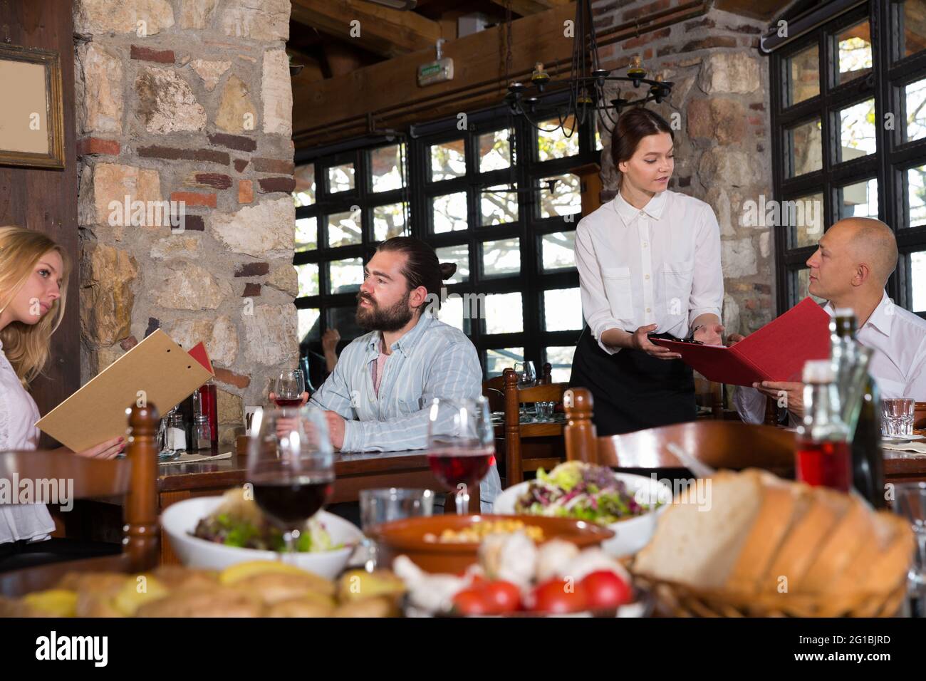 Charming young waiter receiving order from guests in country restaurant ...