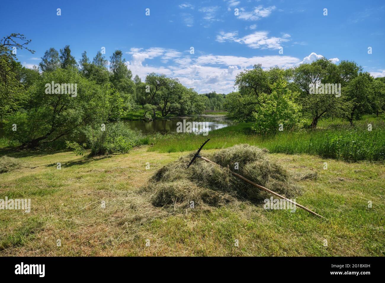 Rake and hay stack on rural landscape. Pond or river on background ...