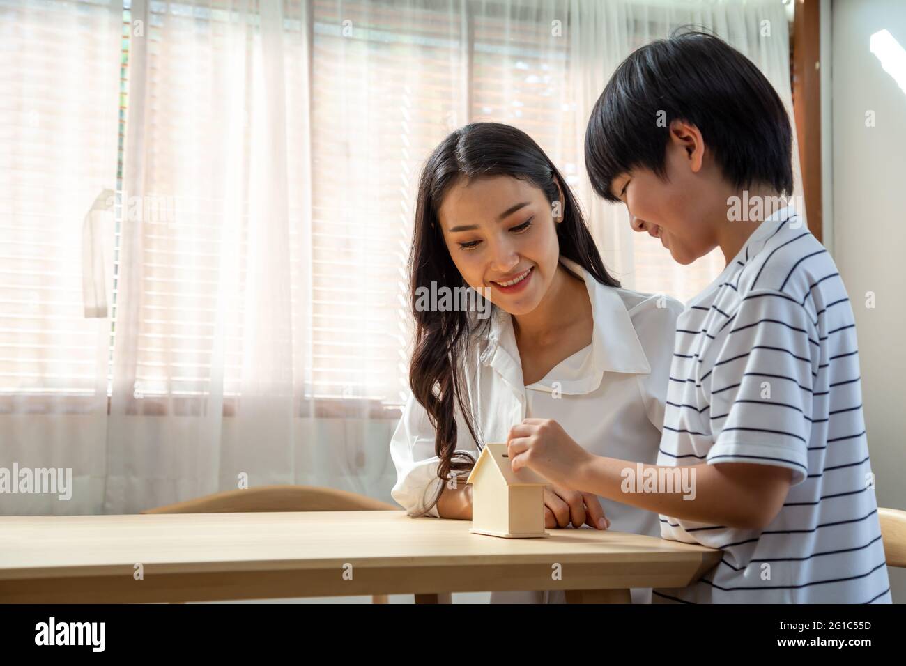 Asian mother and son putting coins into bank home model, Saving money ...