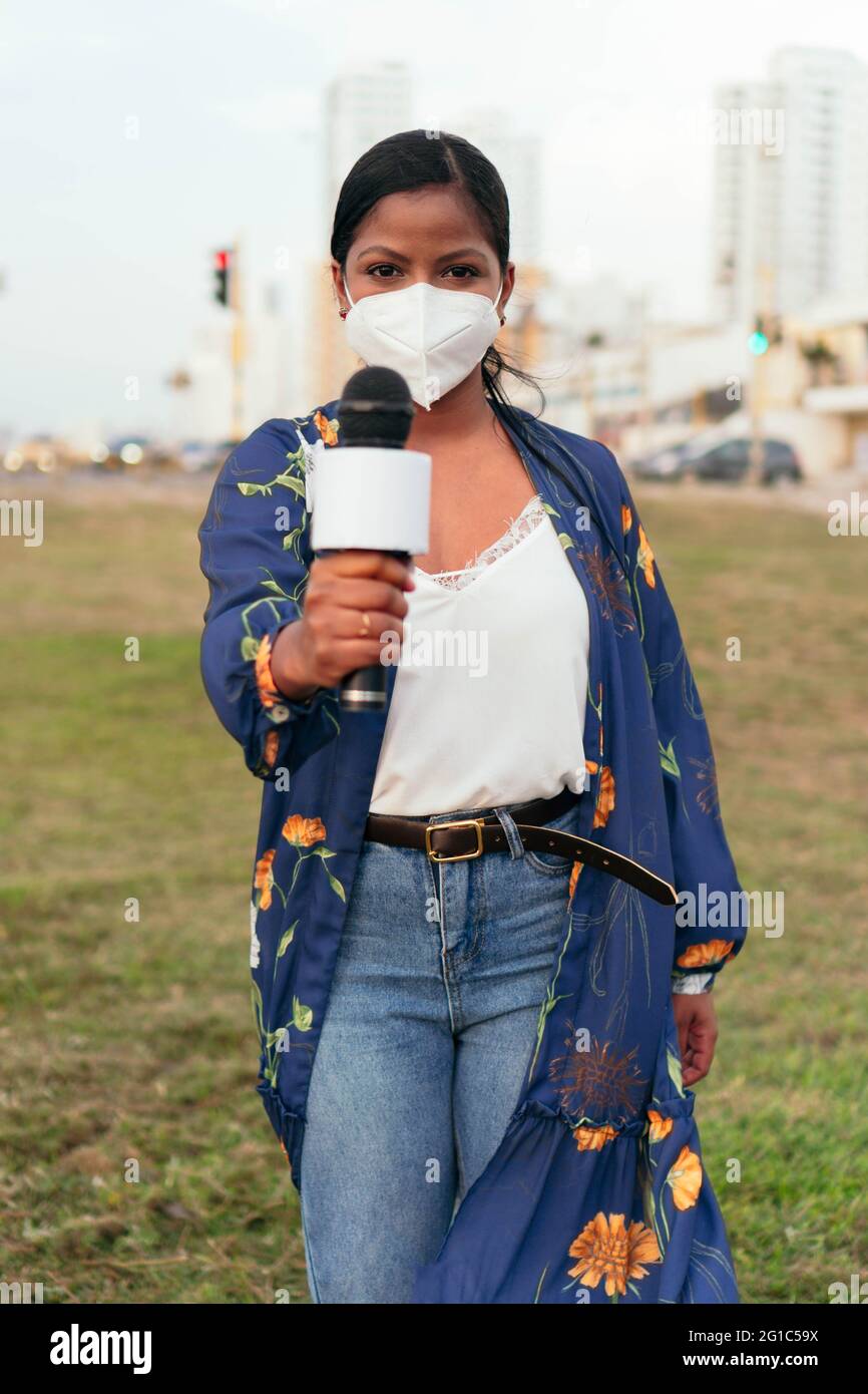 Female journalist wearing mask holding microphone while standing on ...