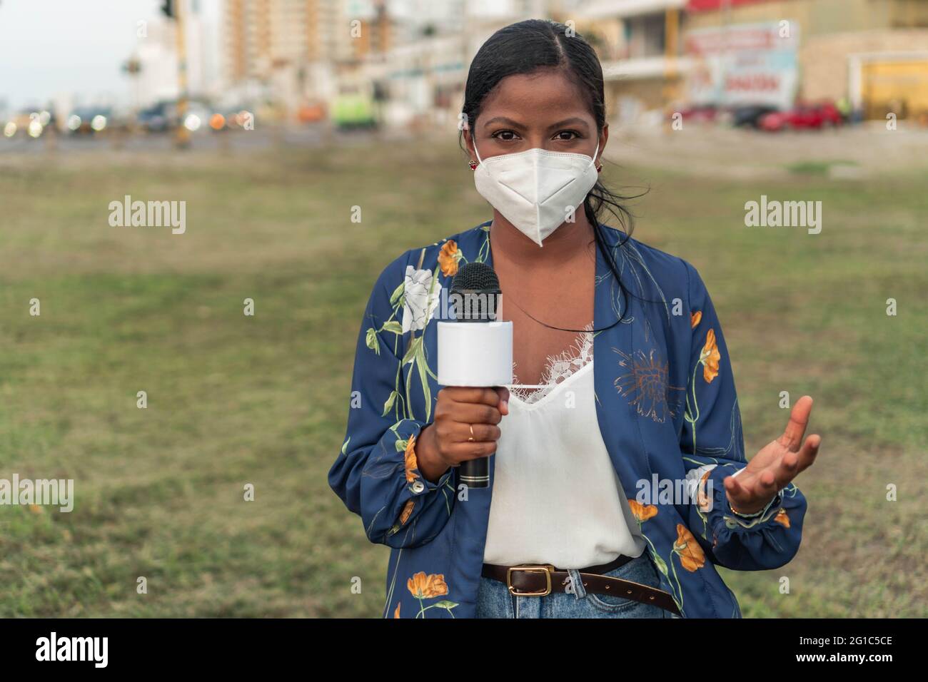 Black woman reporter in mask speaking into microphone while standing on ...