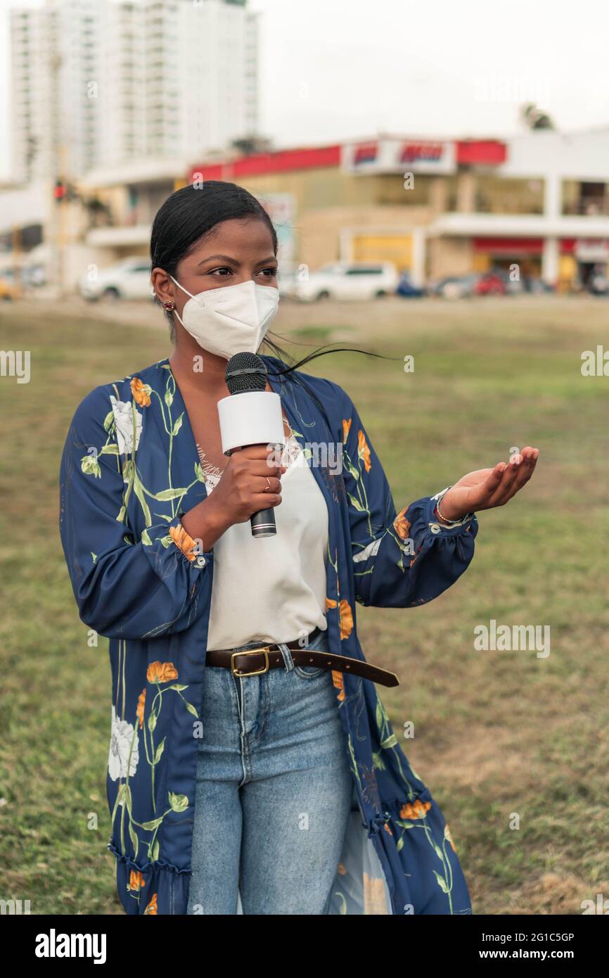 African woman reporter in mask speaking into microphone on the street ...