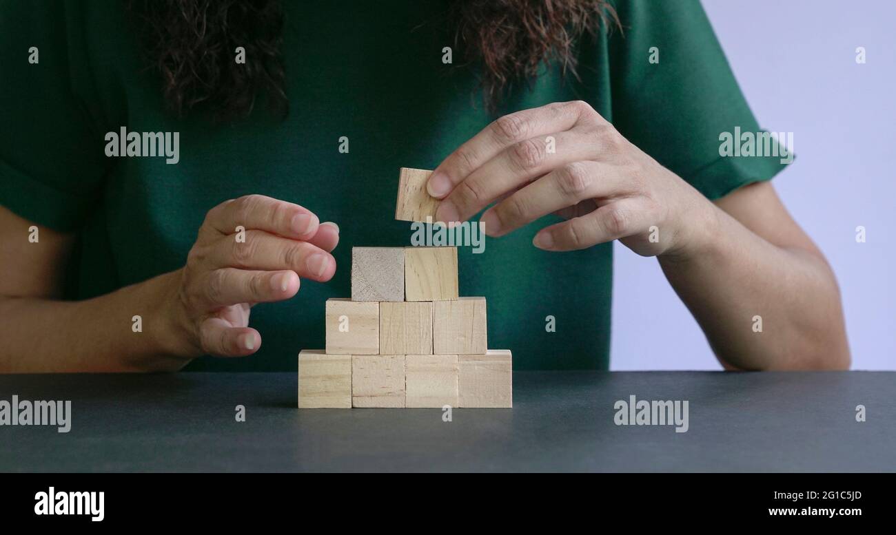 Woman hand putting a square wood block on pyramid stack of wood blocks ...