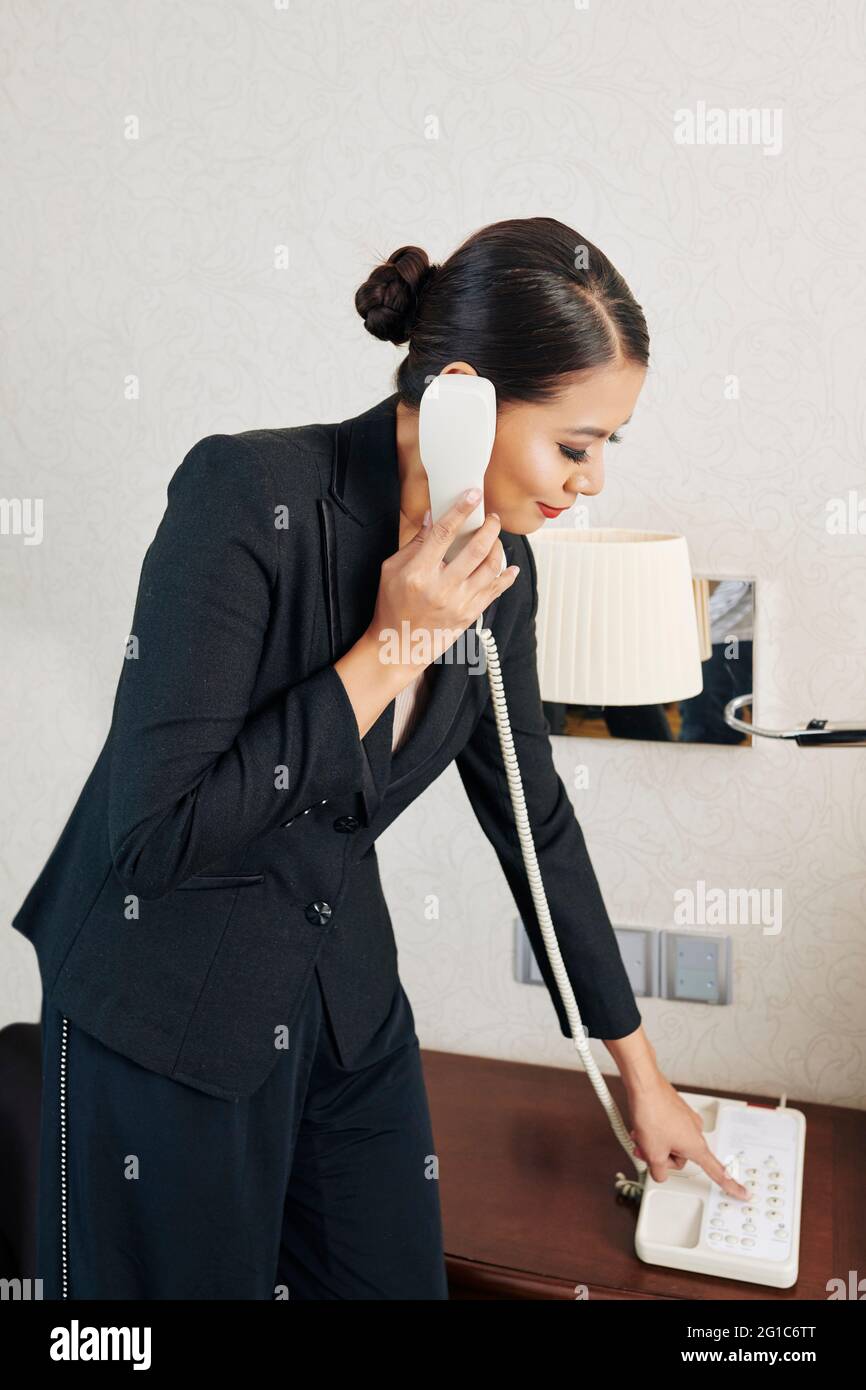 Smiling elegant young woman making phone call from hotel room to ask ...