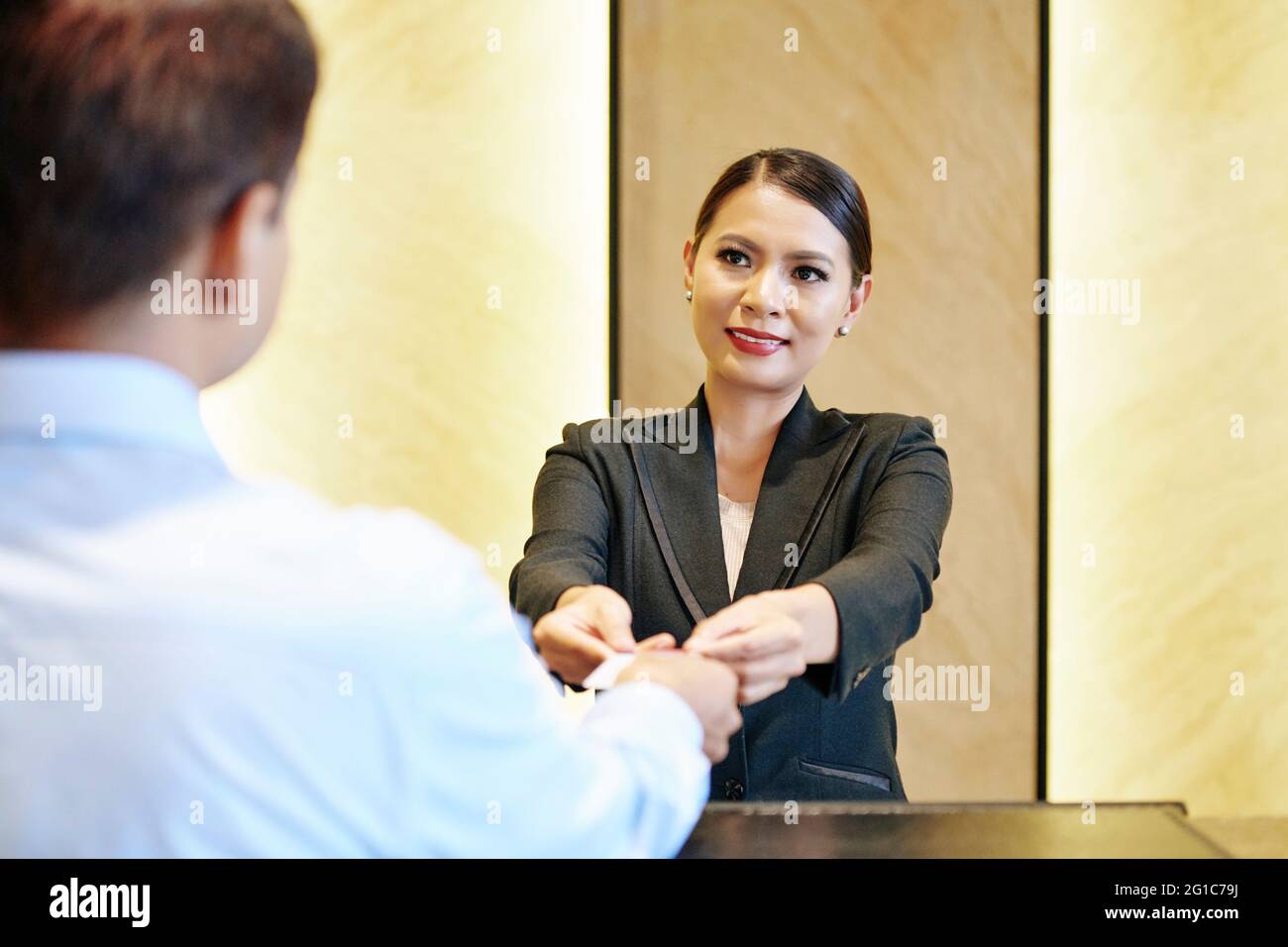 Smiling receptionist giving electronic key card to hotel guest with two ...