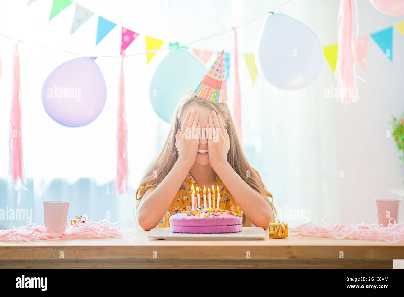 Caucasian girl is dreamily smiling and looking at birthday rainbow cake ...
