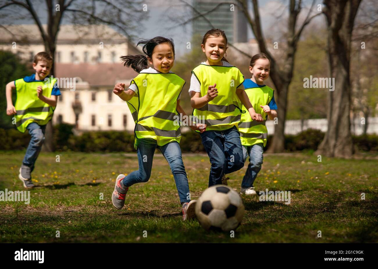 Small children playing football outdoors in city park, learning group ...