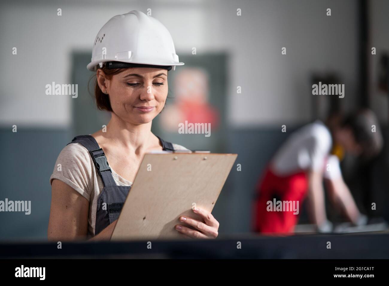 Portrait of woman worker with helmet and clipboard indoors in factory ...