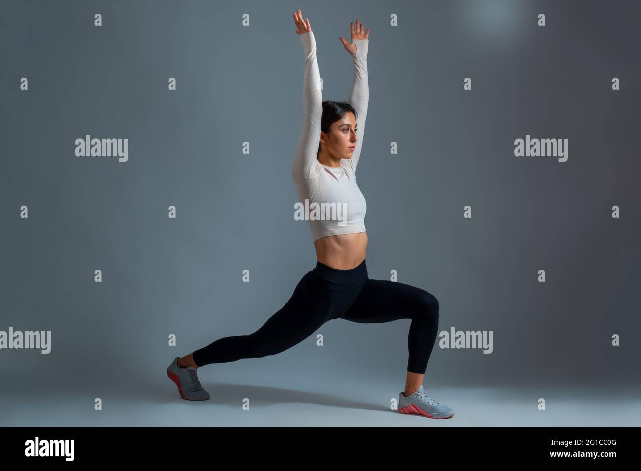 Woman in lunging Warrior Pose with arms outstretched up on grey ...