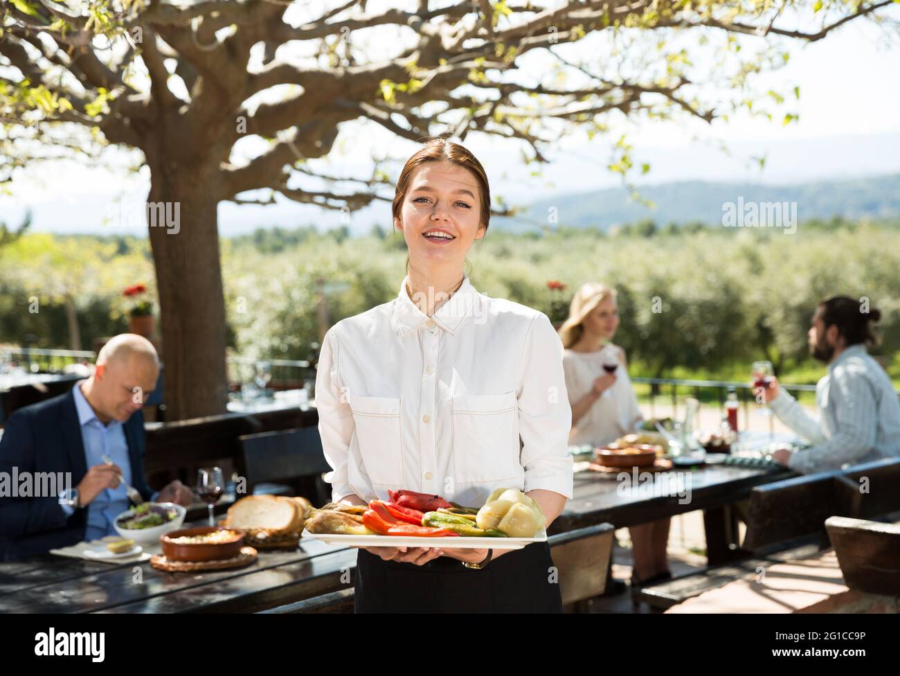 Positive woman waiter demonstrating open-air restaurant to visitors ...