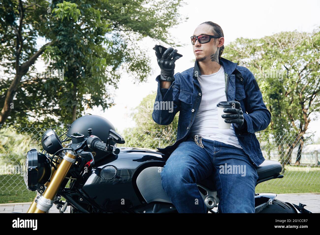 Motorcyclist in sunglasses drinking take out coffee and recording voice ...