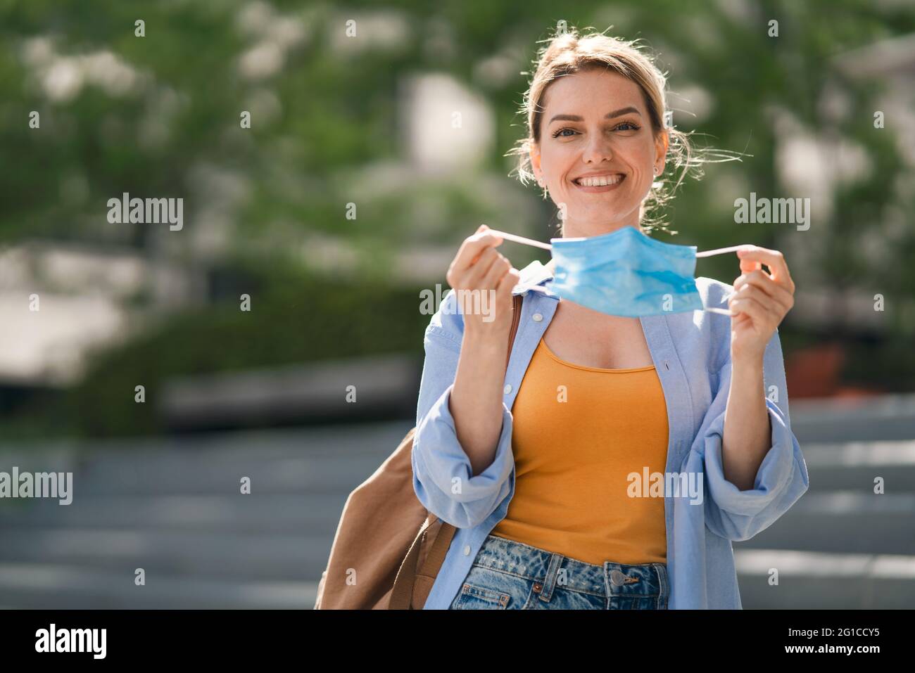 Portrait of young woman taking off face mask outdoors in city, life ...