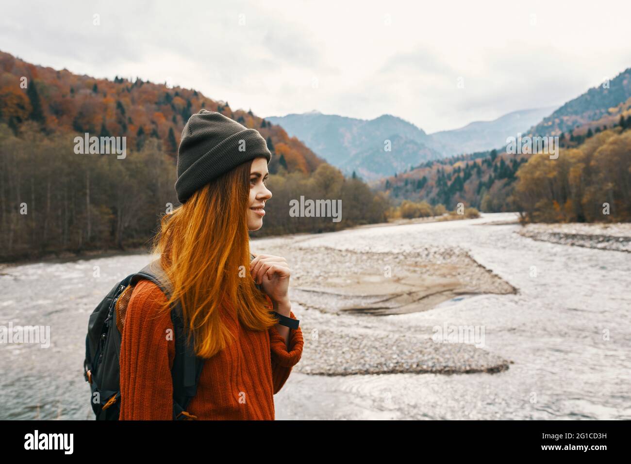 red-haired woman in a sweater with a backpack and in a hat near a ...