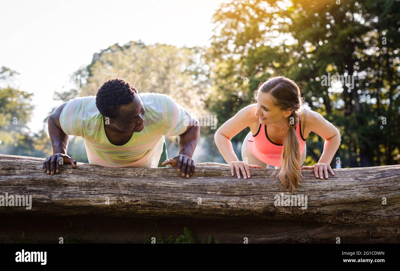 Woman and her fitness coach doing push-ups on tree trunk in summer ...