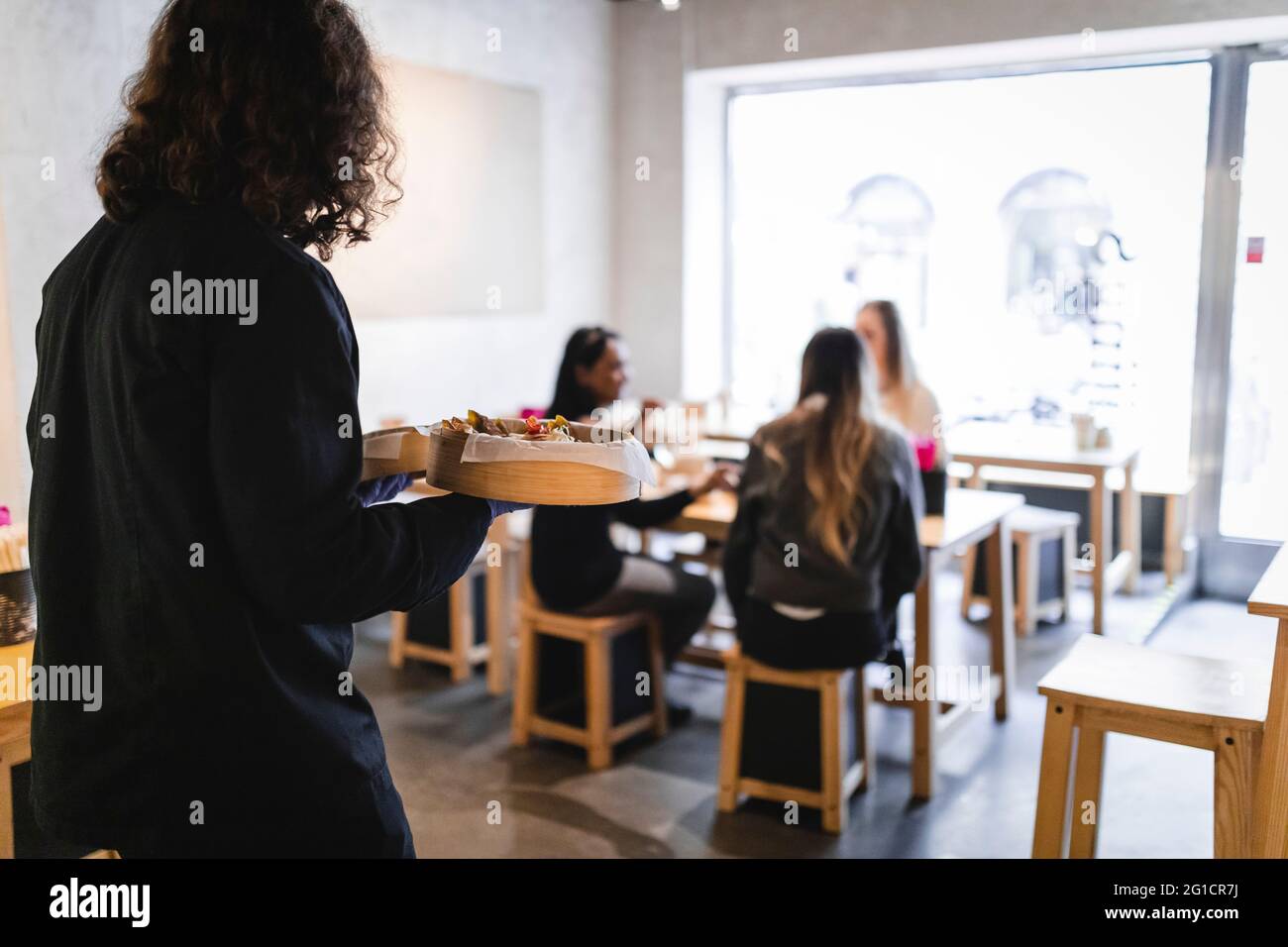 Rear view of male waiter serving food to female customers in restaurant ...