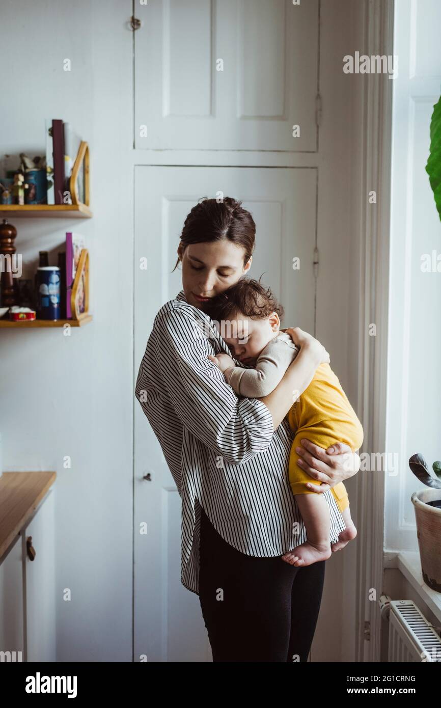 Mother carrying baby boy while standing at home Stock Photo - Alamy