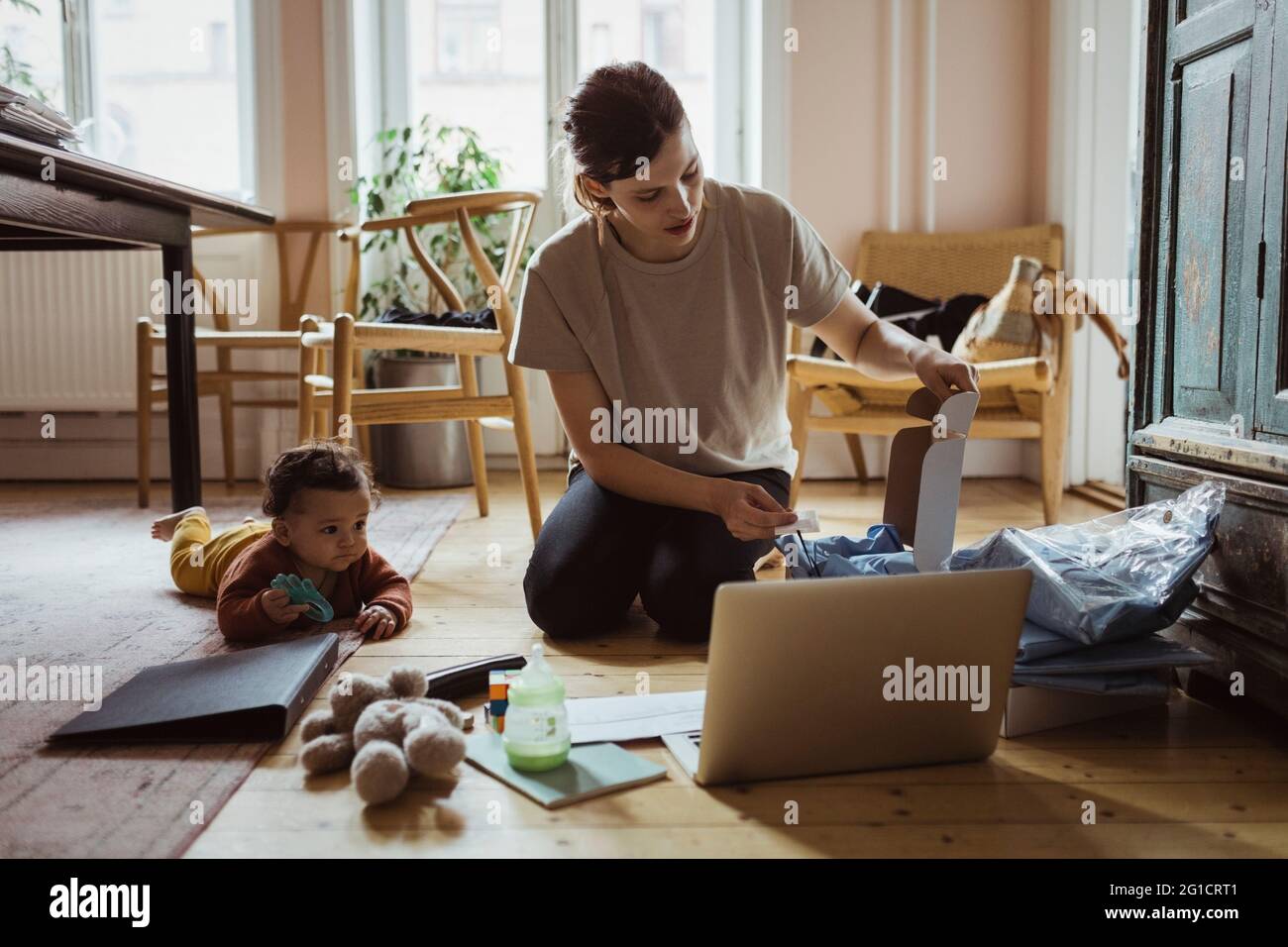 Female entrepreneur packing shirt in box by toddler son at home Stock ...