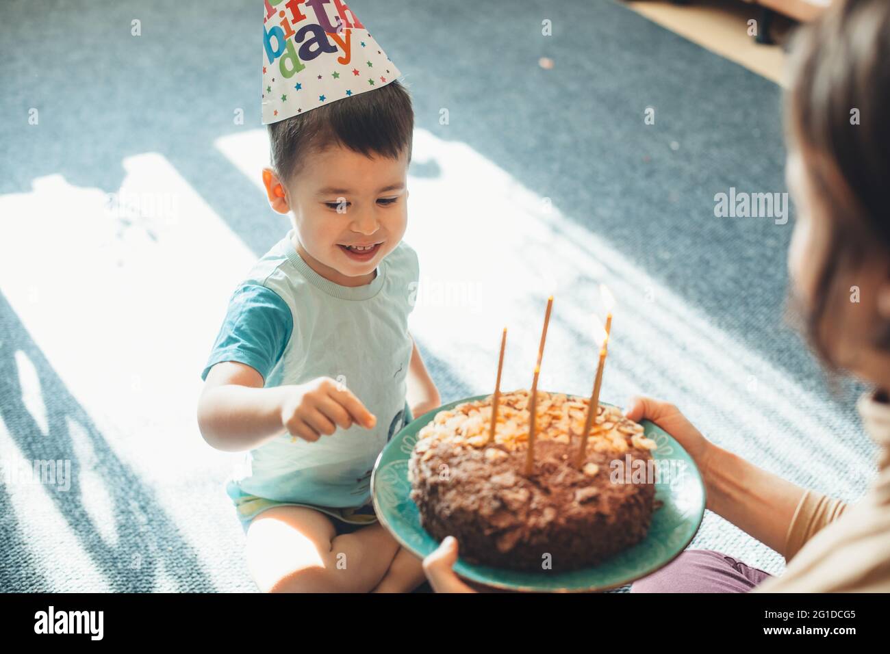 Adorable kid is wearing party hat while mother is giving him a birthday ...