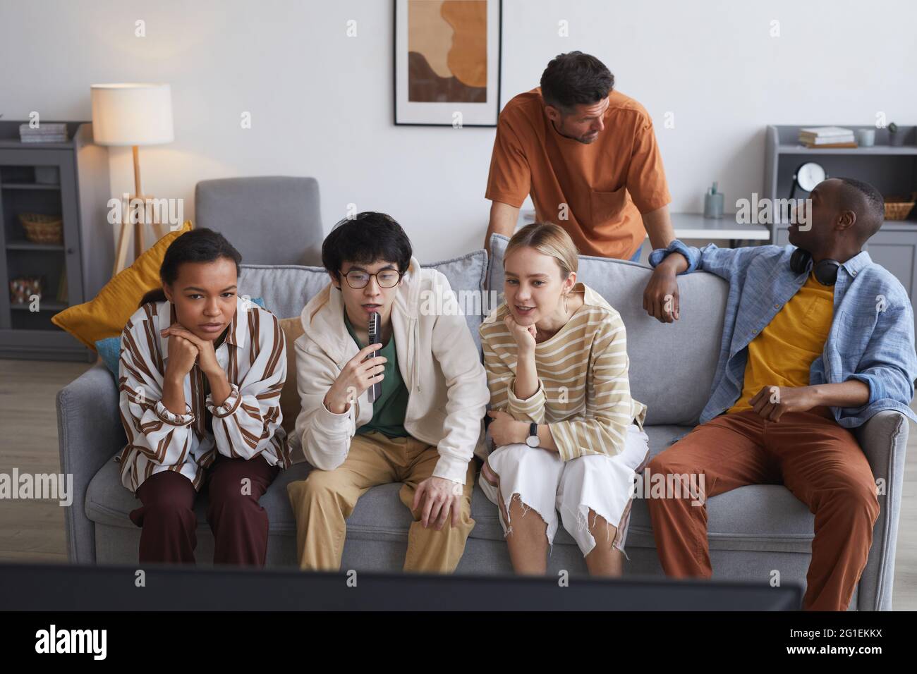 Diverse group of friends watching TV at home together while sitting on ...