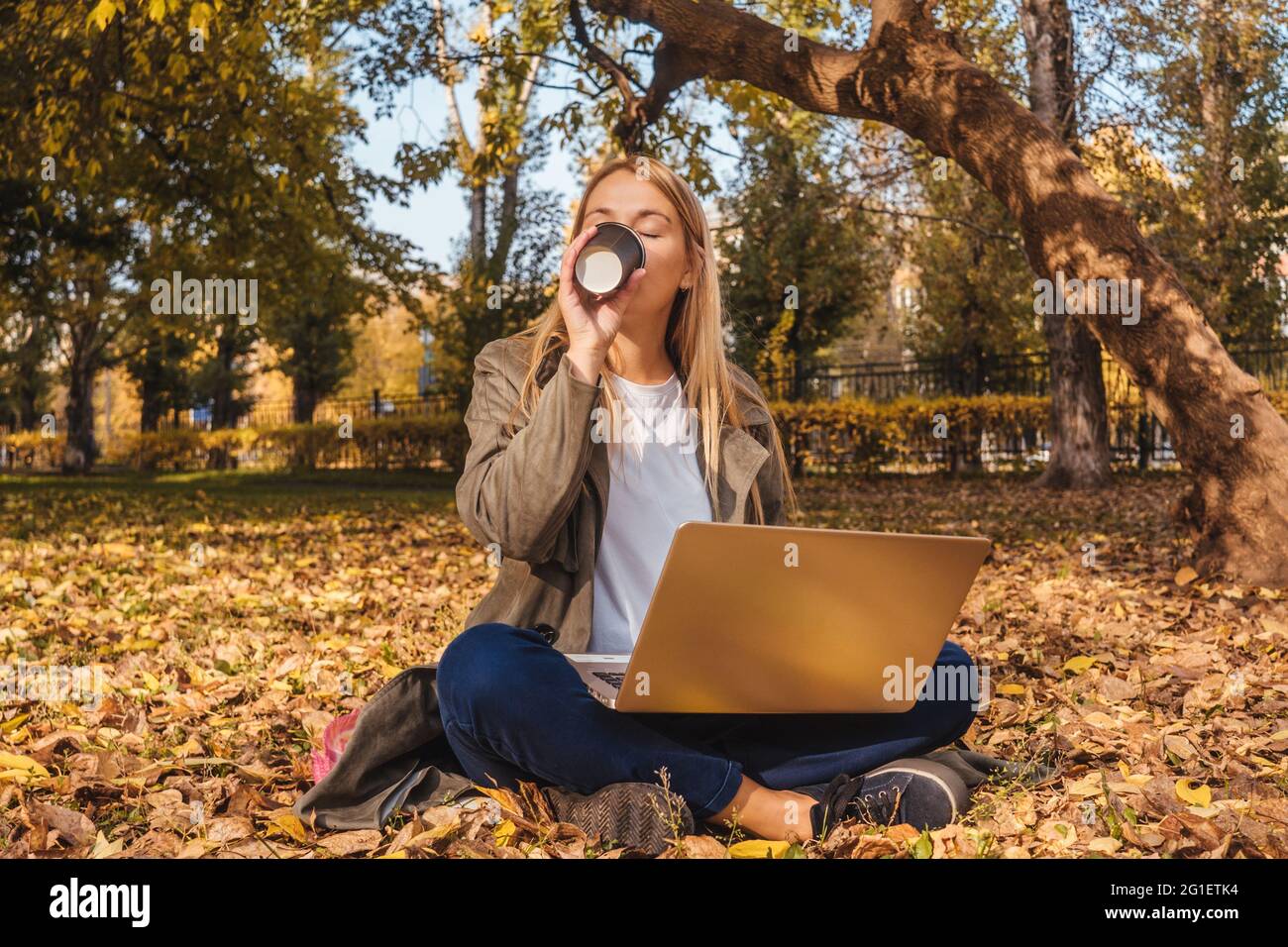 Young businesswoman working on laptop on nature and drink coffee ...
