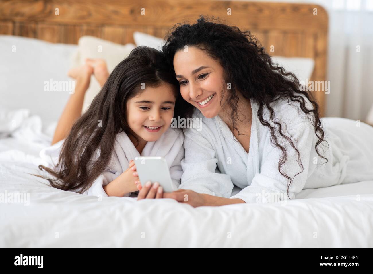Cheerful mother and daughter in bathrobes using smartphone Stock Photo - Alamy