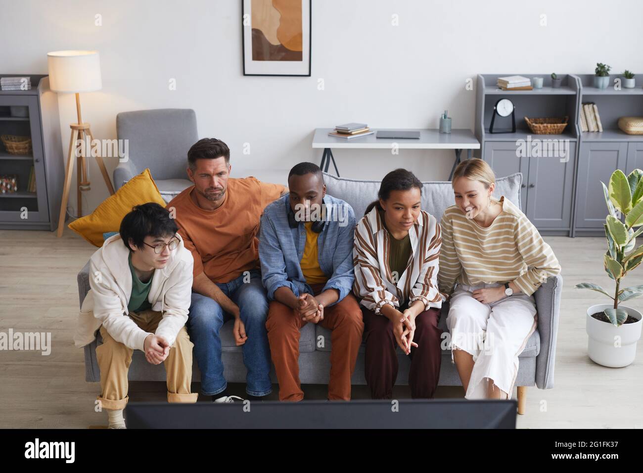 Wide angle view at multi-ethnic group of friends watching TV at home ...