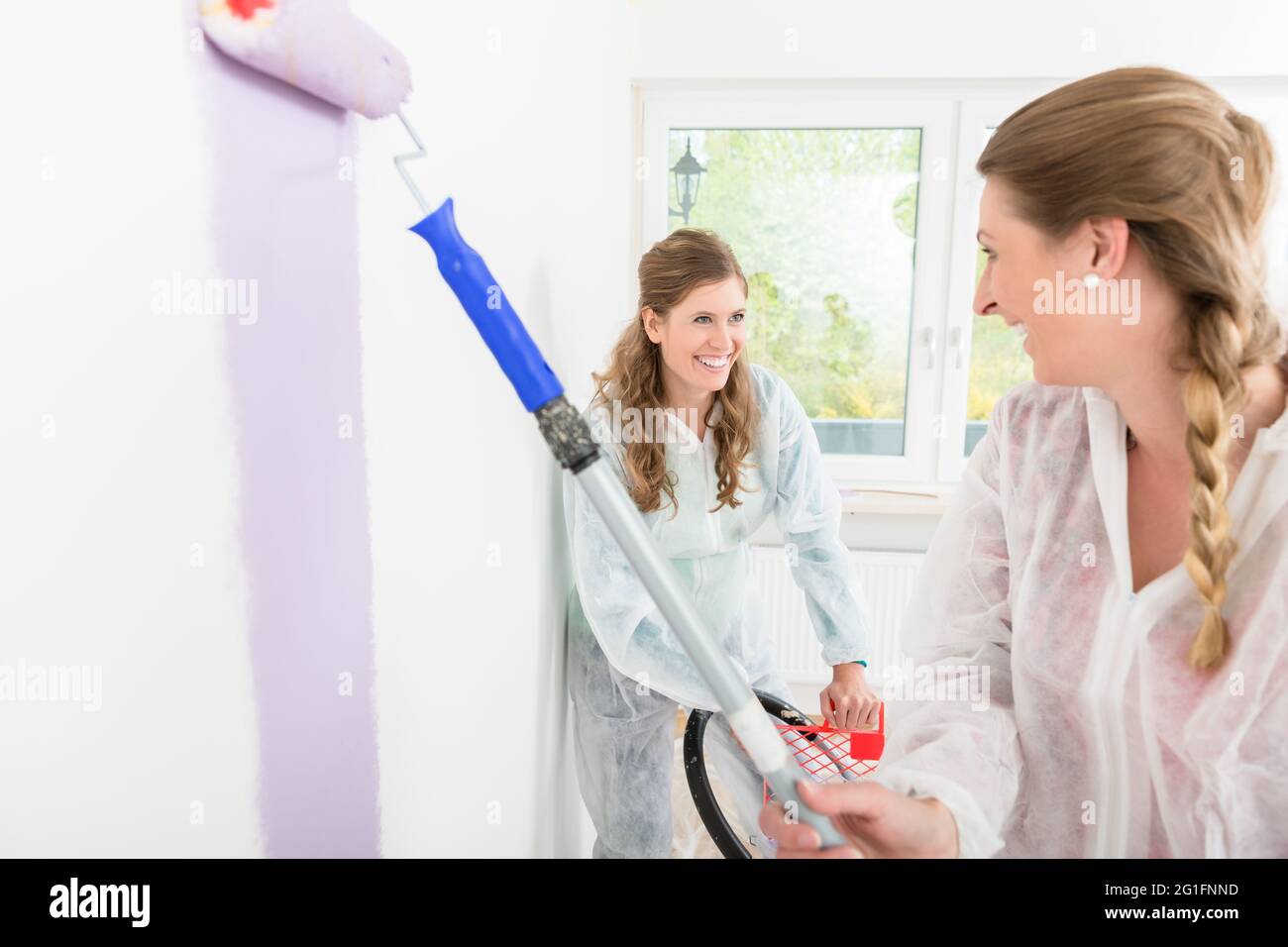 Two friends making fun while painting the new house with roller Stock ...
