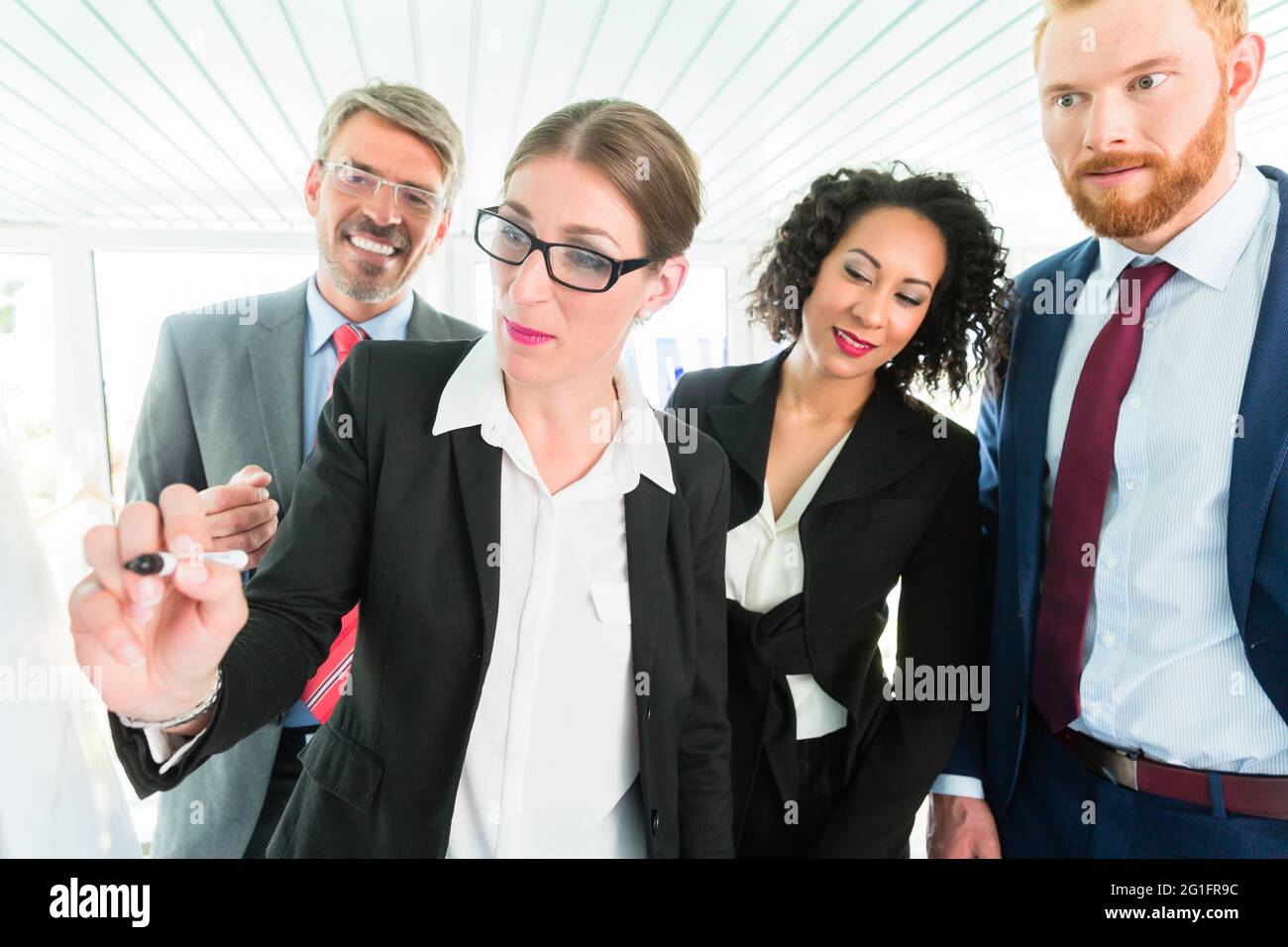 Businesswoman writes on a flipboard in front of three co-workers Stock ...
