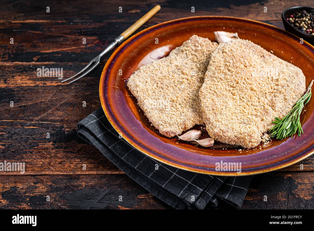 Raw Breaded German Wiener schnitzel on a rustic plate with herbs. Dark ...