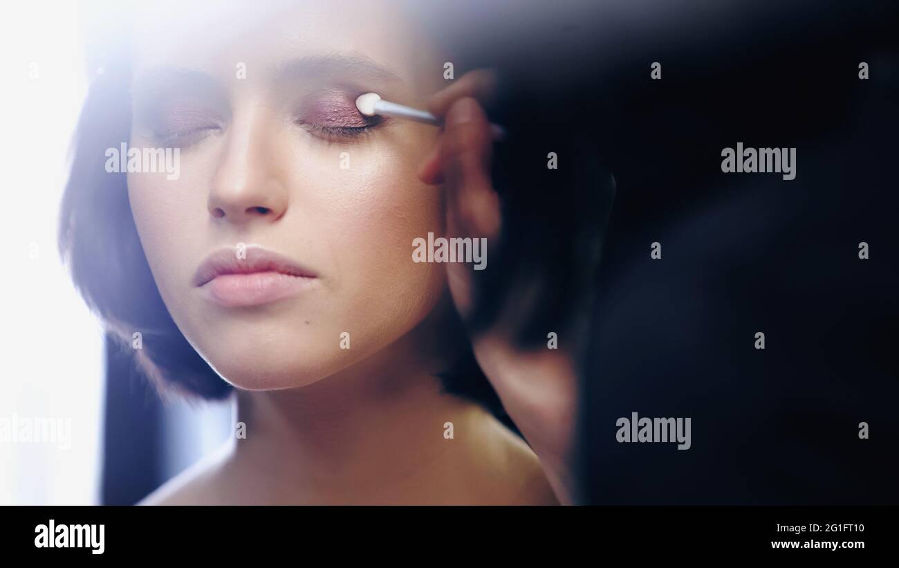 makeup artist applying eye shadow with cosmetic brush on woman with ...