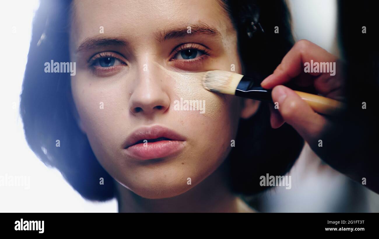 makeup artist holding cosmetic brush while applying makeup foundation ...