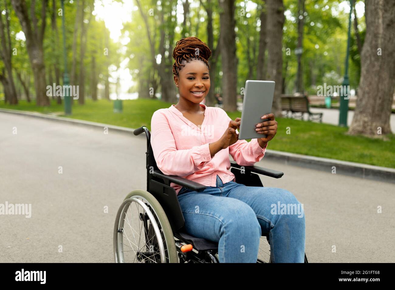 Happy impaired young woman in wheelchair using tablet computer for ...