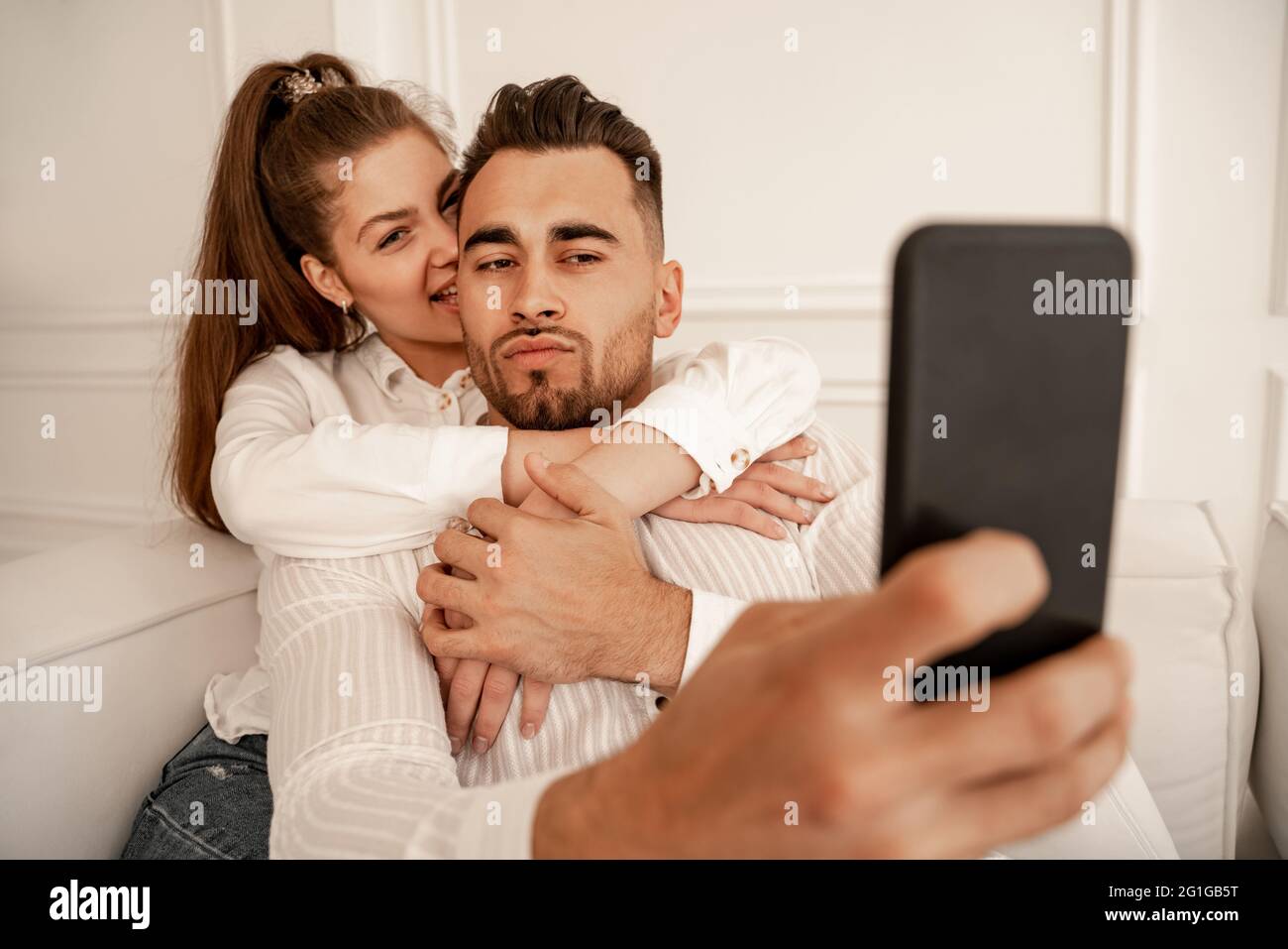 joyful woman biting ear of boyfriend taking selfie on smartphone on ...