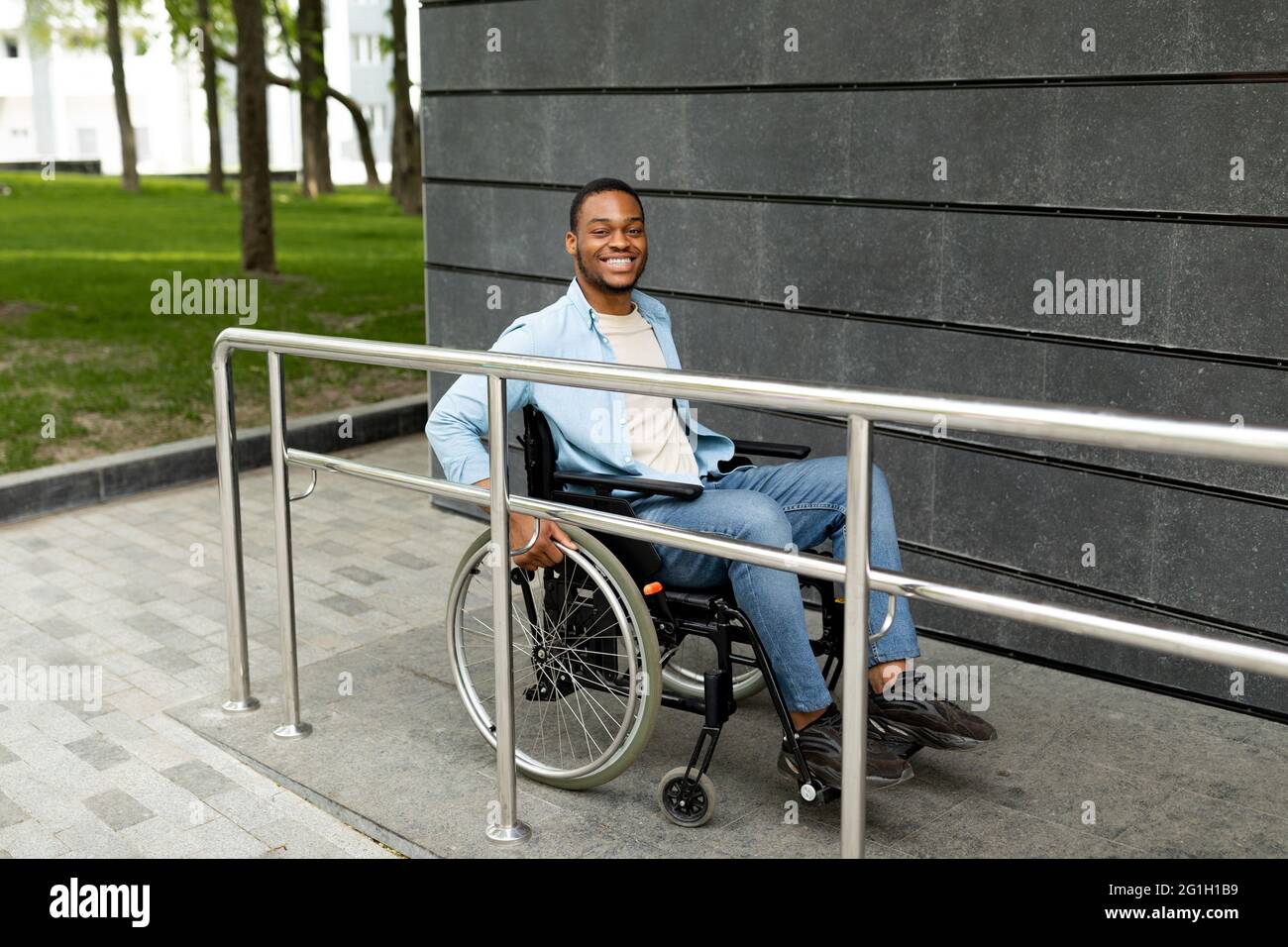 Happy impaired black man in wheelchair entering building on ramp ...