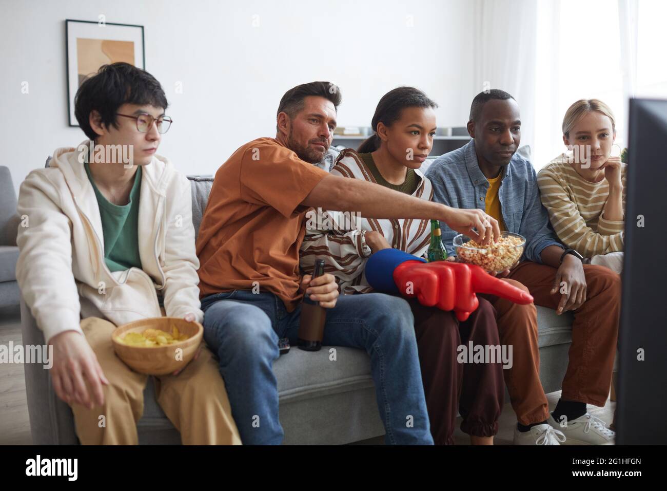 Diverse group of sports fans watching game match at home and eating ...