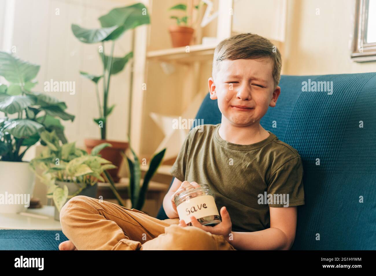 Sad crying Little child kid boy putting stack coins in to glass jar ...