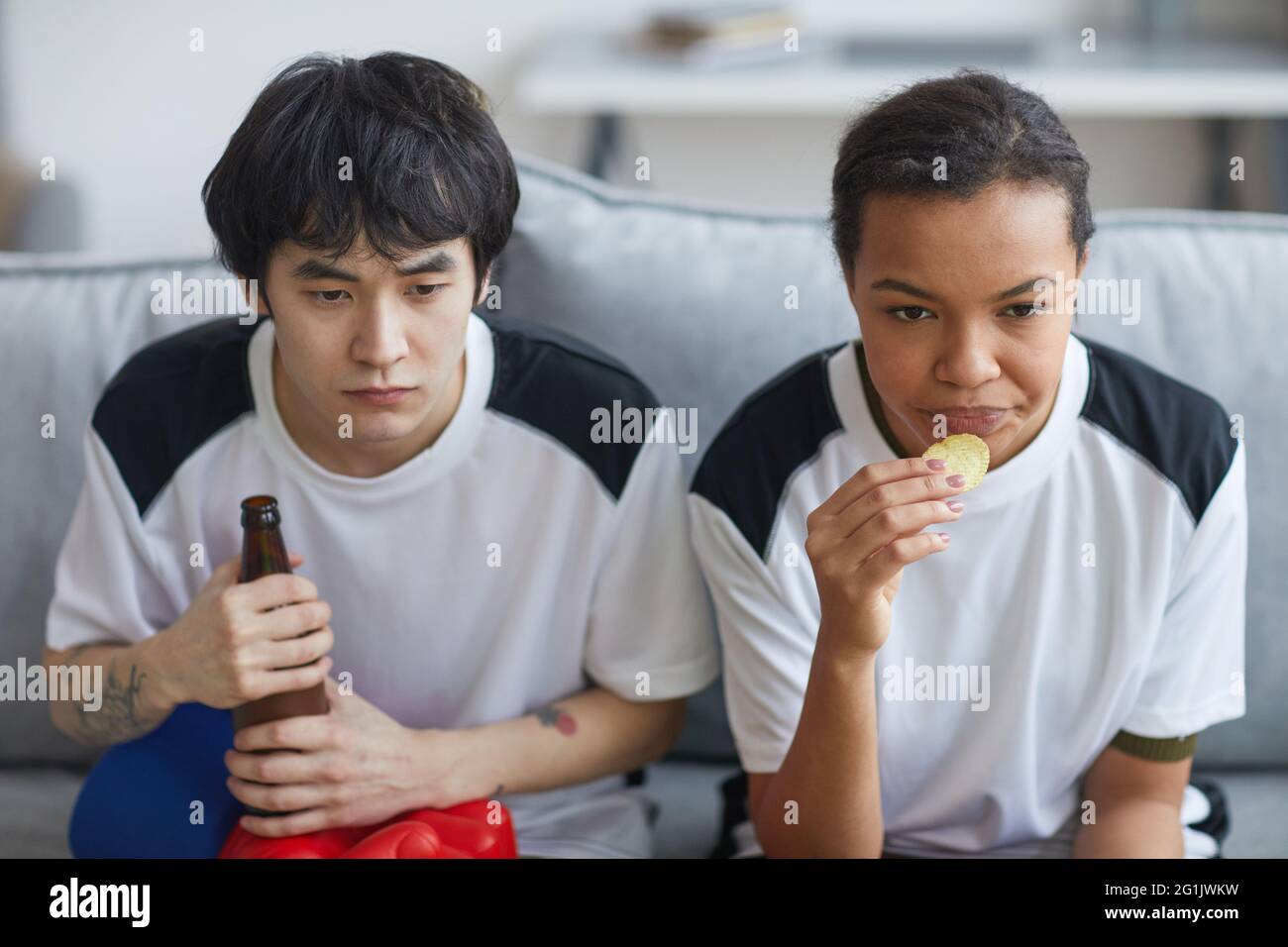 High angle view at two young people watching Tv and eating snacks at ...