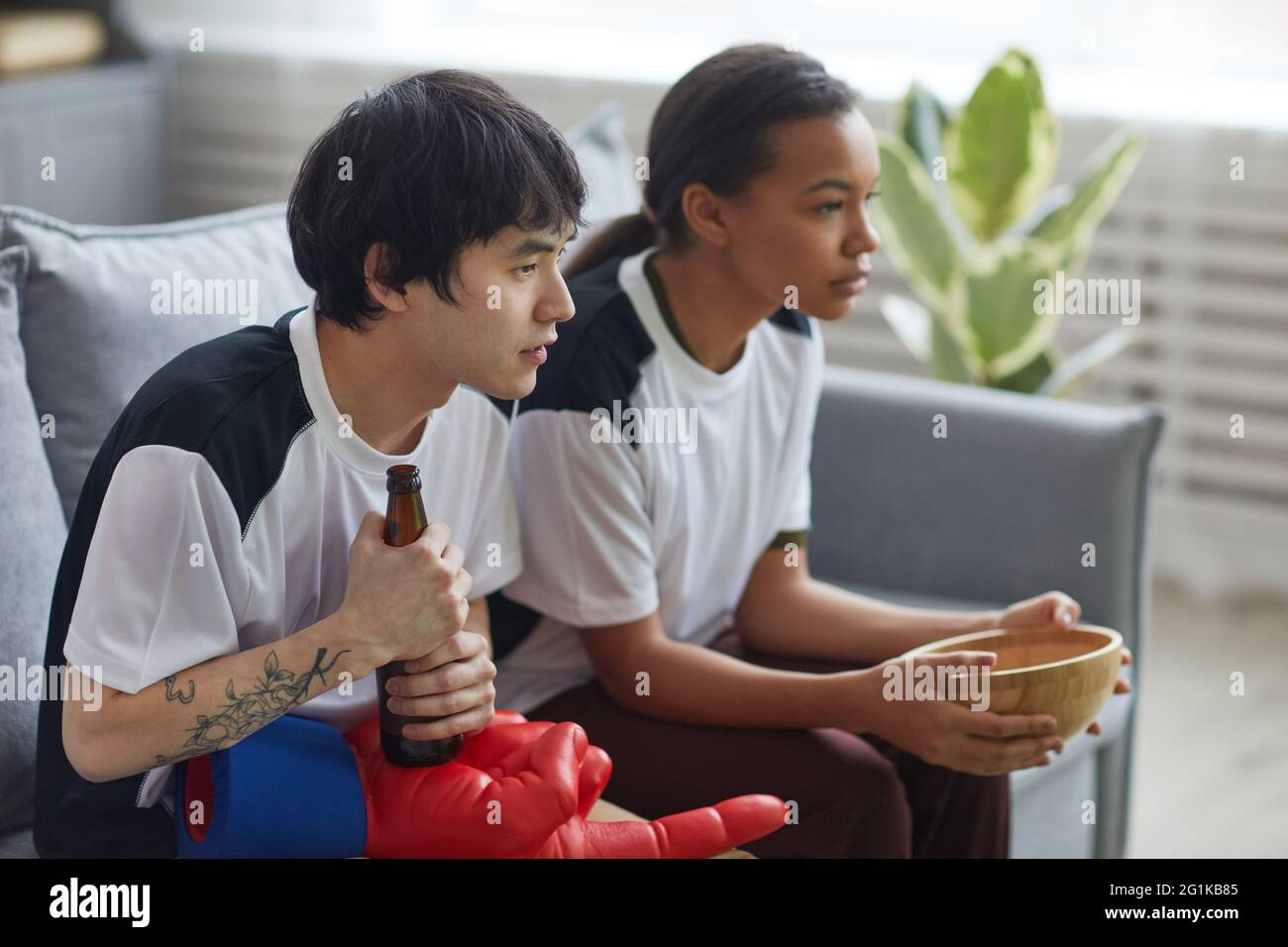 Side view at two young people watching TV and eating snacks at home ...