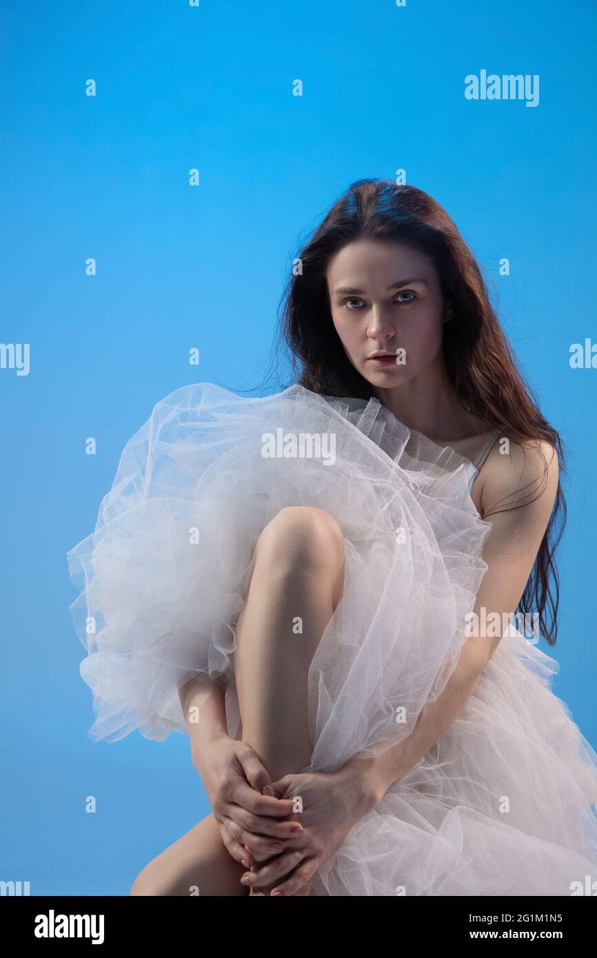 Tired ballet dancer sitting over blue studio background Stock Photo - Alamy