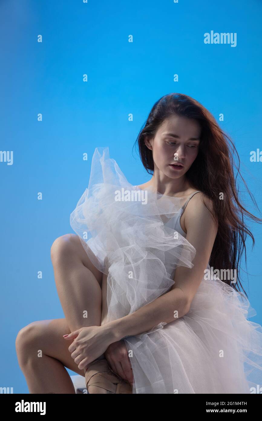 Tired ballet dancer sitting over blue studio background Stock Photo - Alamy