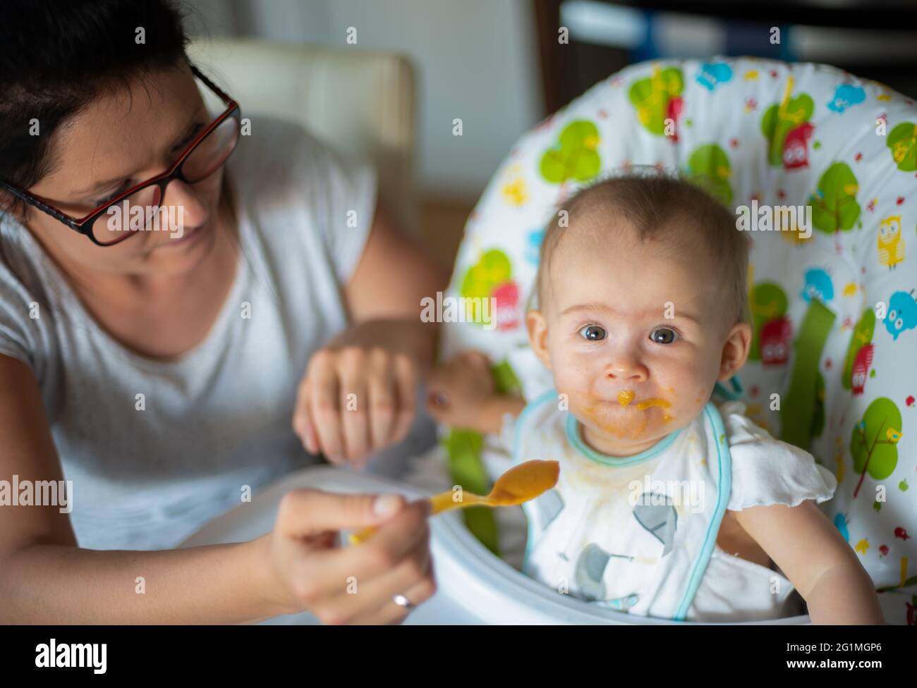 mom giving homogenized food to her daughter on high chair Stock Photo ...