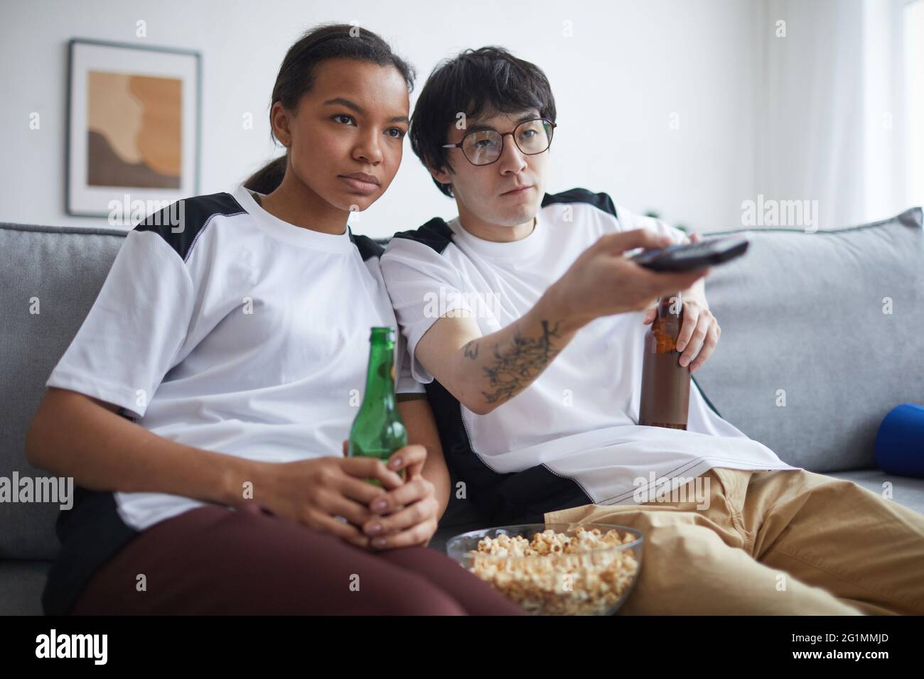 Portrait of two young people watching TV at home and switching channels ...