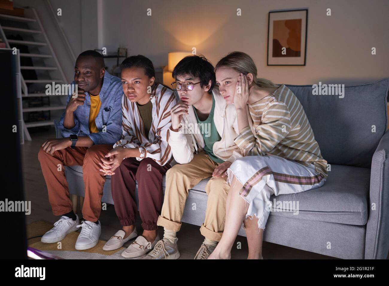 Full length portrait of diverse group of friends watching TV at home ...