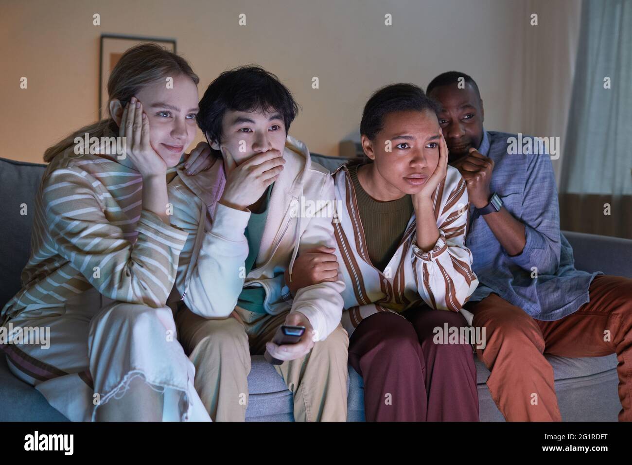 Diverse group of friends watching TV at home lit by blue light with ...