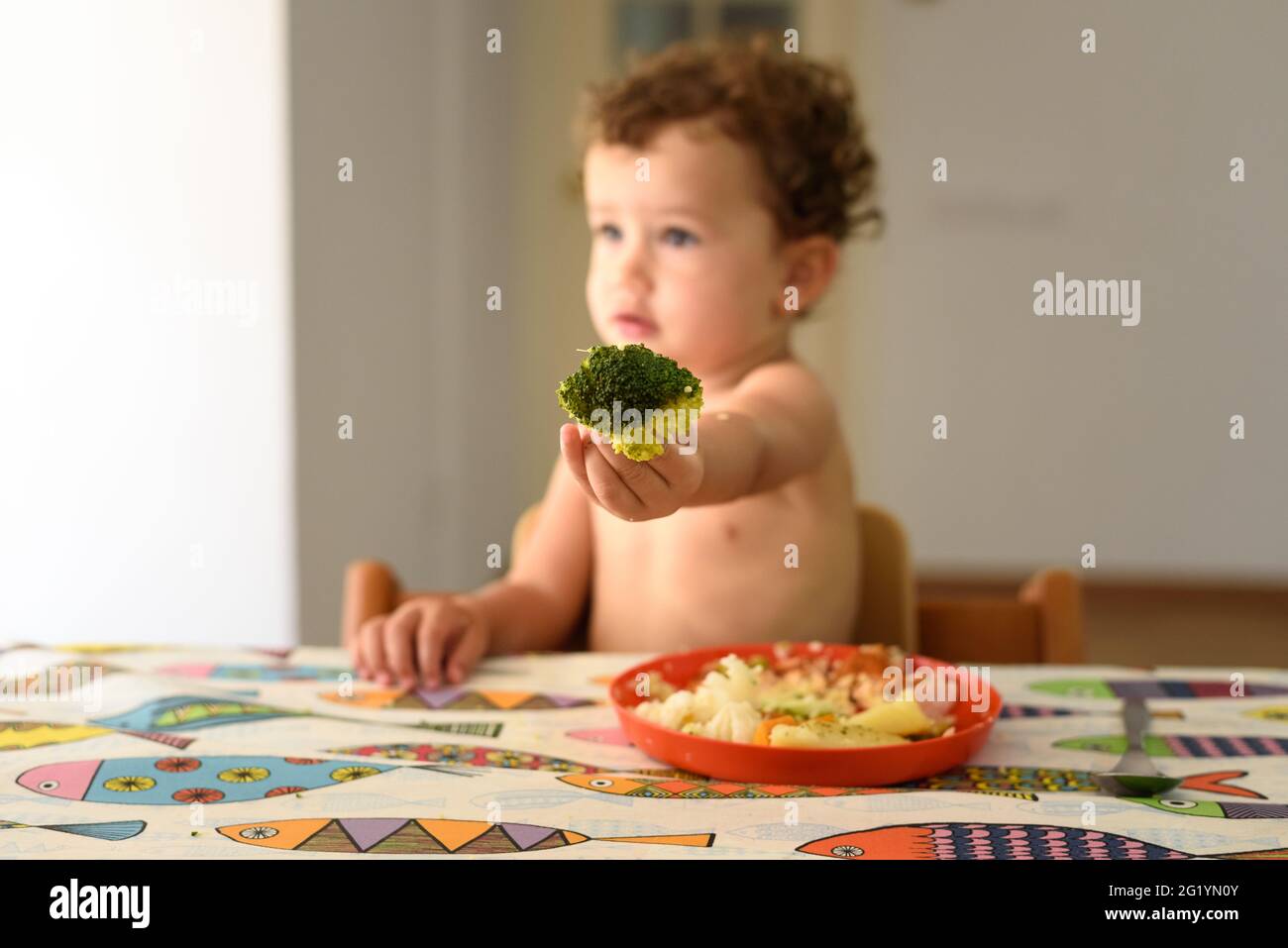 An adorable little girl sitting at the table enjoys eating vegetables ...