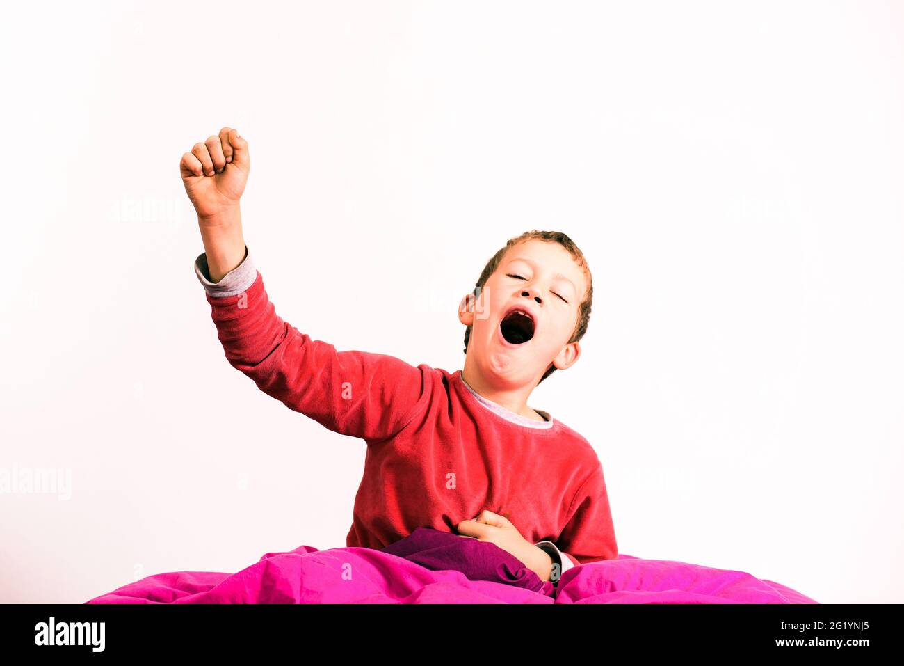 Adorable blond boy yawning just woken up in his bed, isolated on white ...