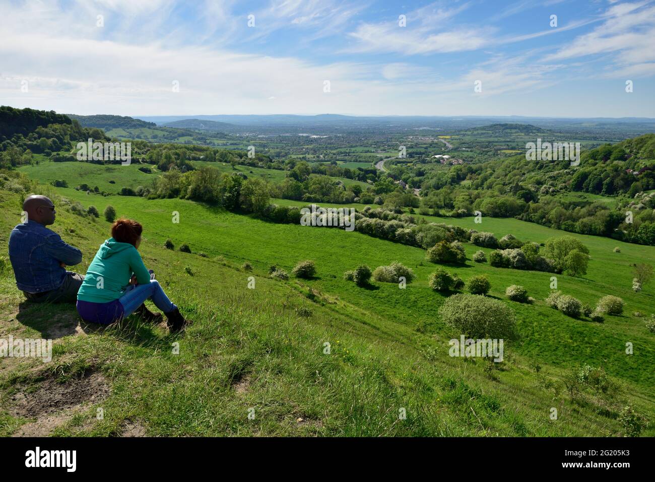 Two people sitting on grassy escarpment above Severn Vale looking ...