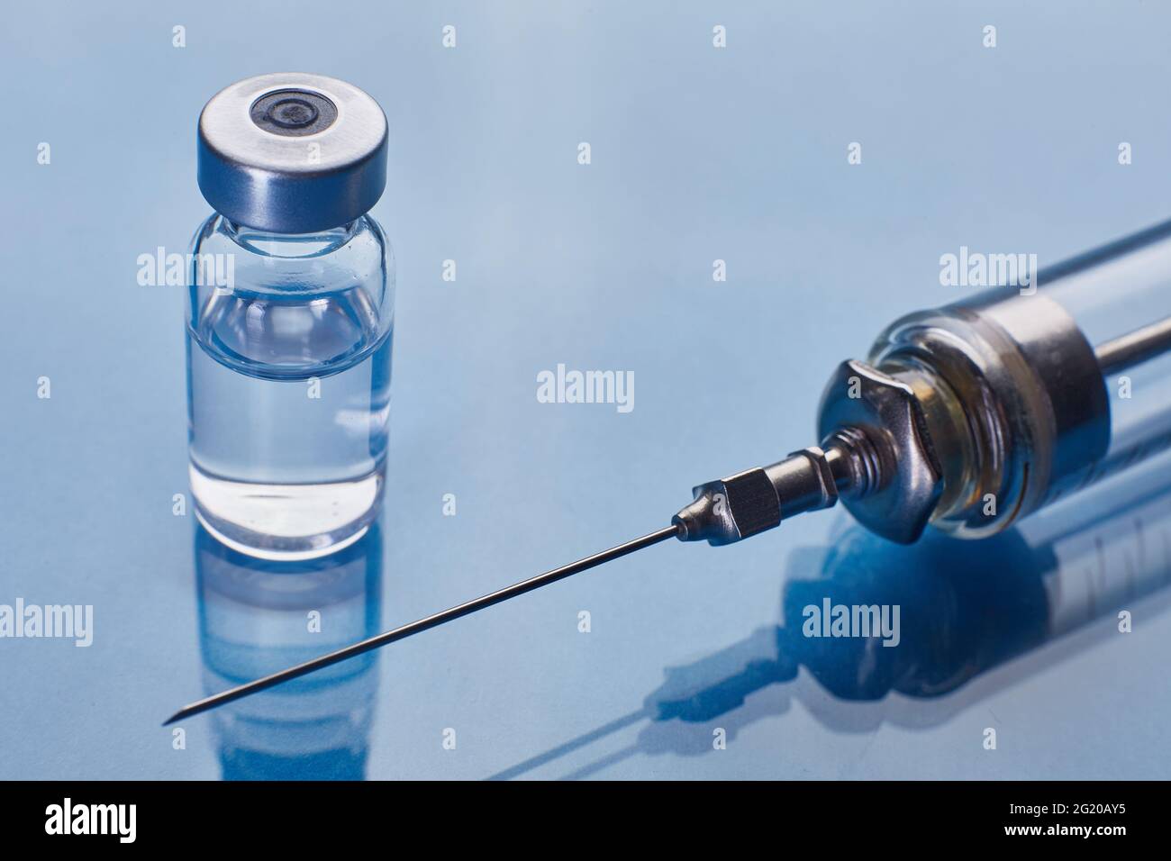 Glass vaccine vial and glass medical syringe on blue glass background ...