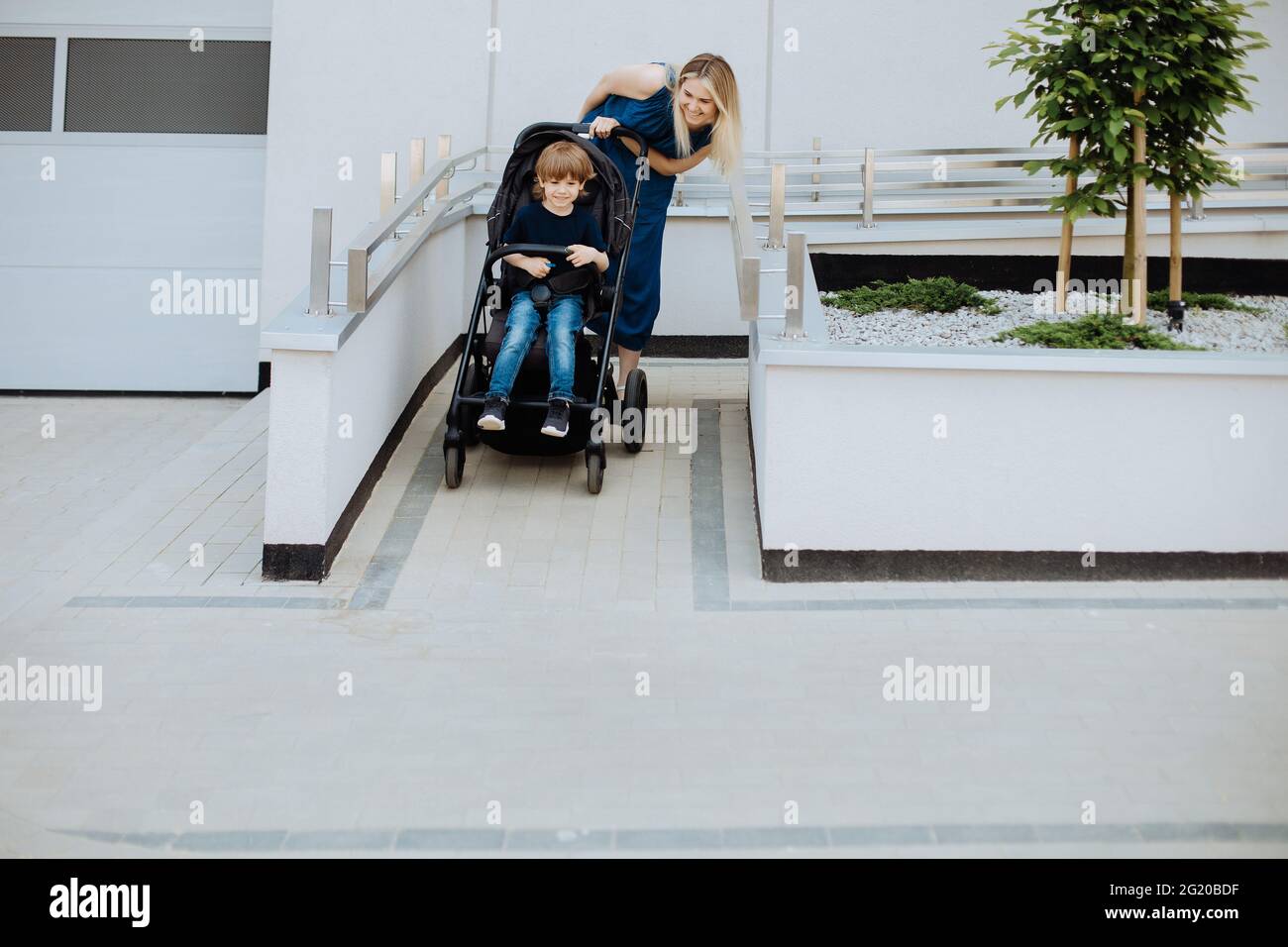 Young beautiful mother is taking her son for walk in stroller. Family ...