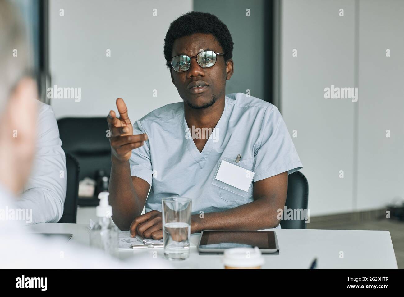 Portrait of young African-American doctor speaking to colleagues during ...